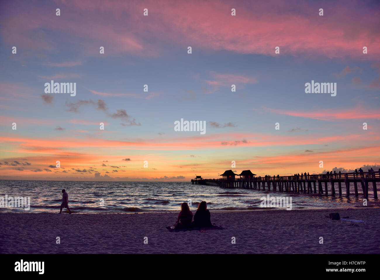 People on sandy beach in near silhouette with Naples historic pier ...