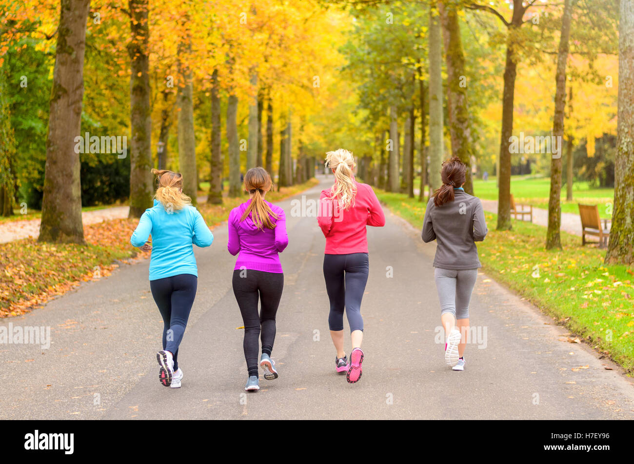 Four female friends running together in autumn along a road through a ...