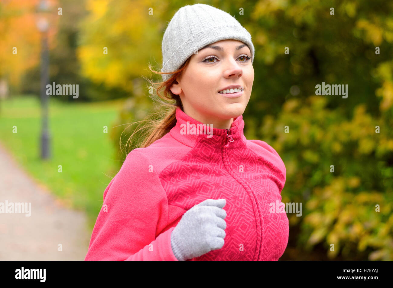 Smiling fit young woman jogging in a colorful fall park in a healthy ...
