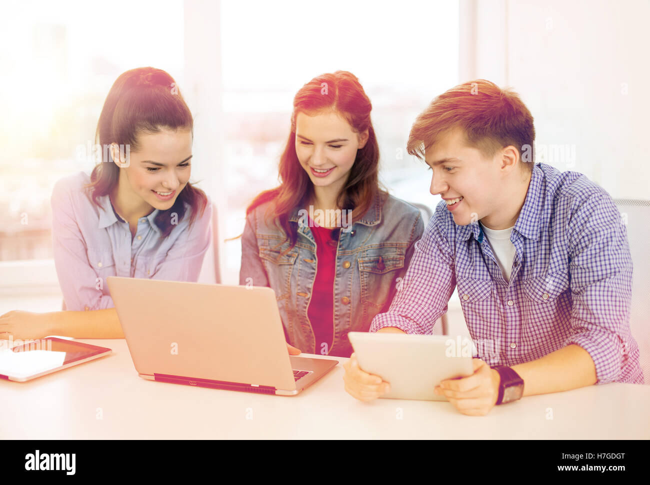 three smiling students with laptop and tablet pc Stock Photo - Alamy