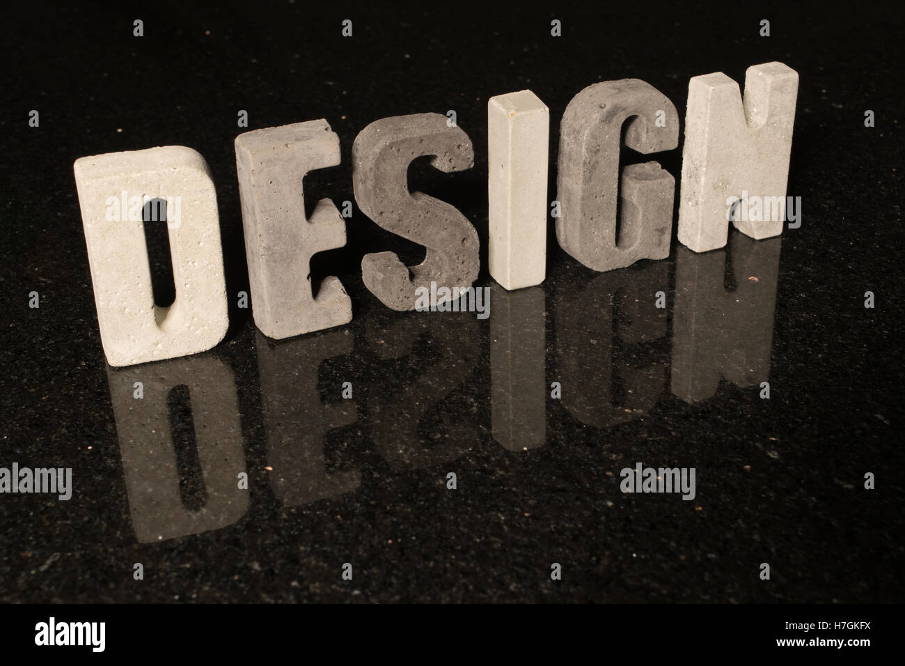 The word Design spelled with grey concrete letters on black reflecting ...