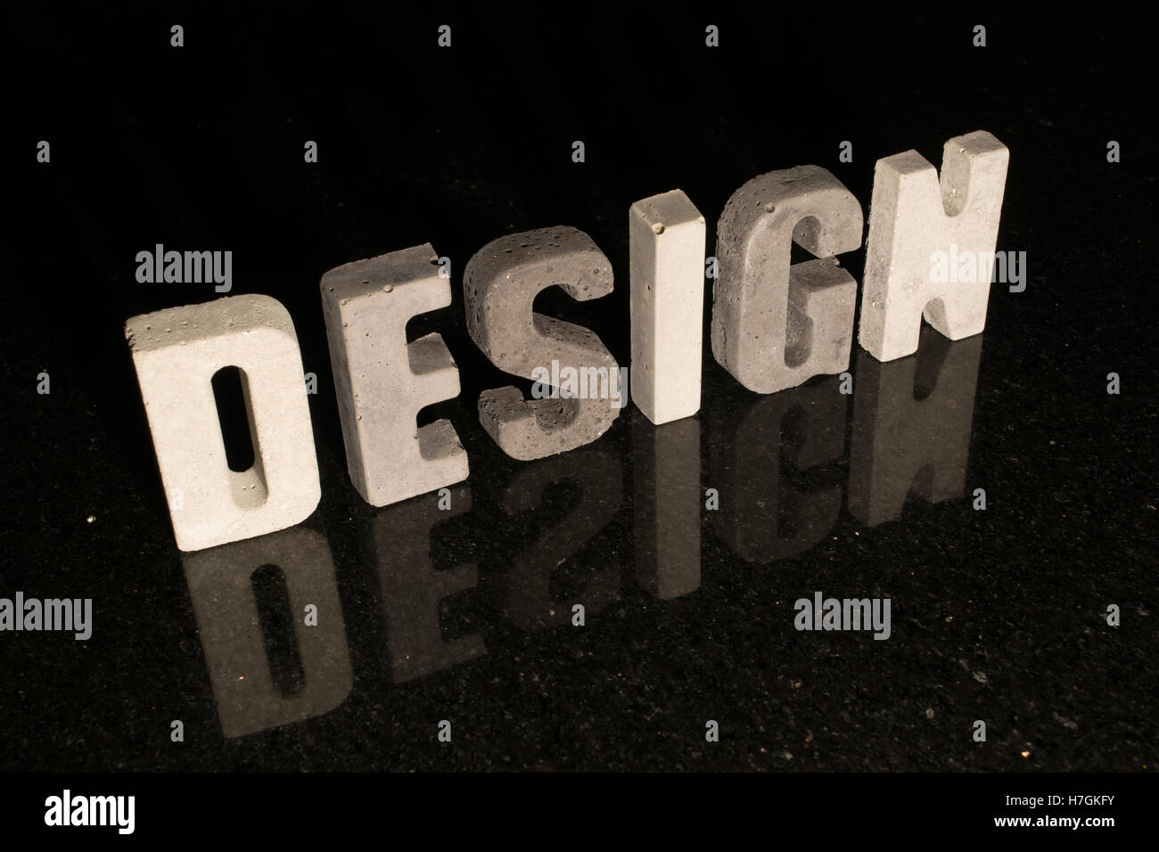 The word Design spelled with grey concrete letters on black reflecting ...