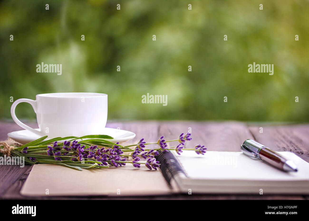blank white notebook, flowers and cup of coffee on the desk outdoors in ...