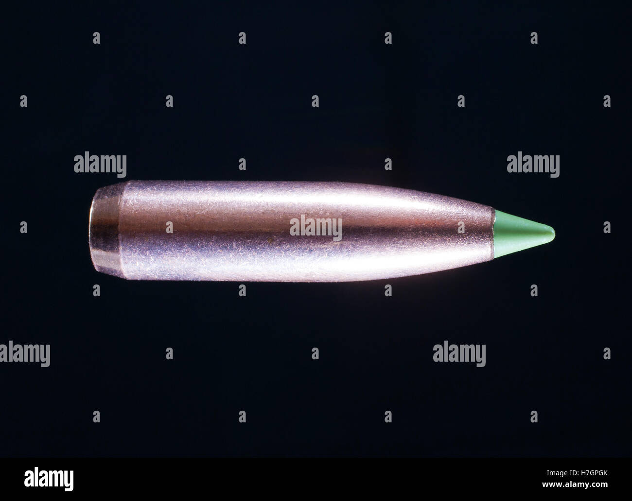 Copper plated bullet with a green polymer tip on a black background ...