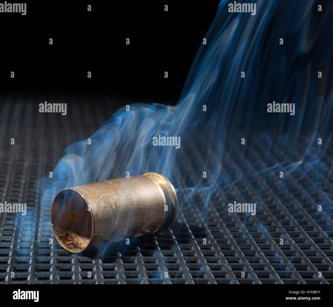 Empty handgun shell on a black grate with smoke nearby Stock Photo - Alamy