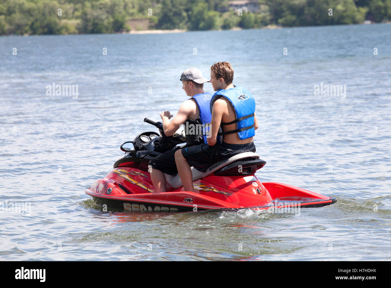 Two teenage boys wearing life vests driving Sea-Doo personal watercraft ...