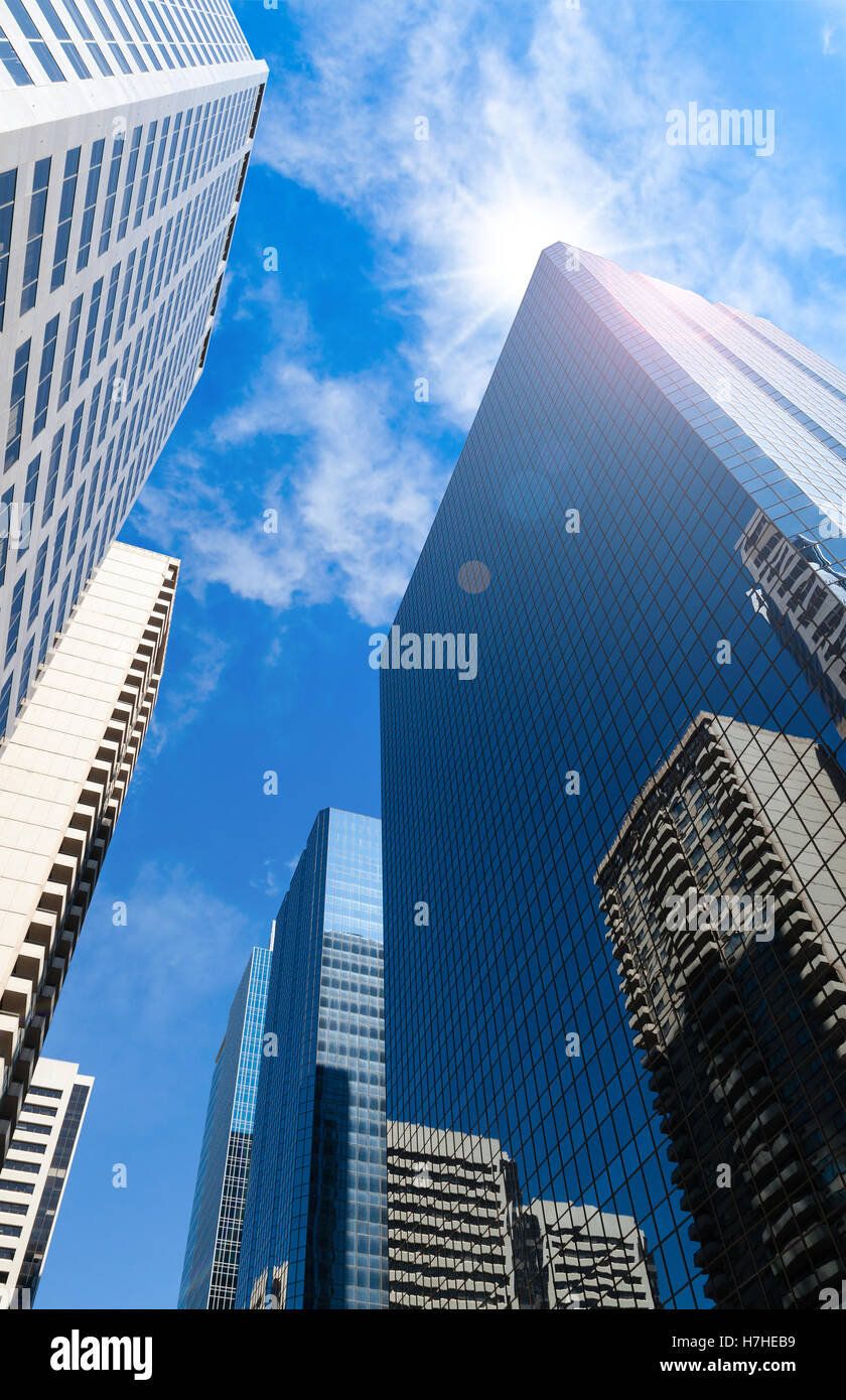 Tall skyscrapers against a blue sky with sun peeking through creating a ...