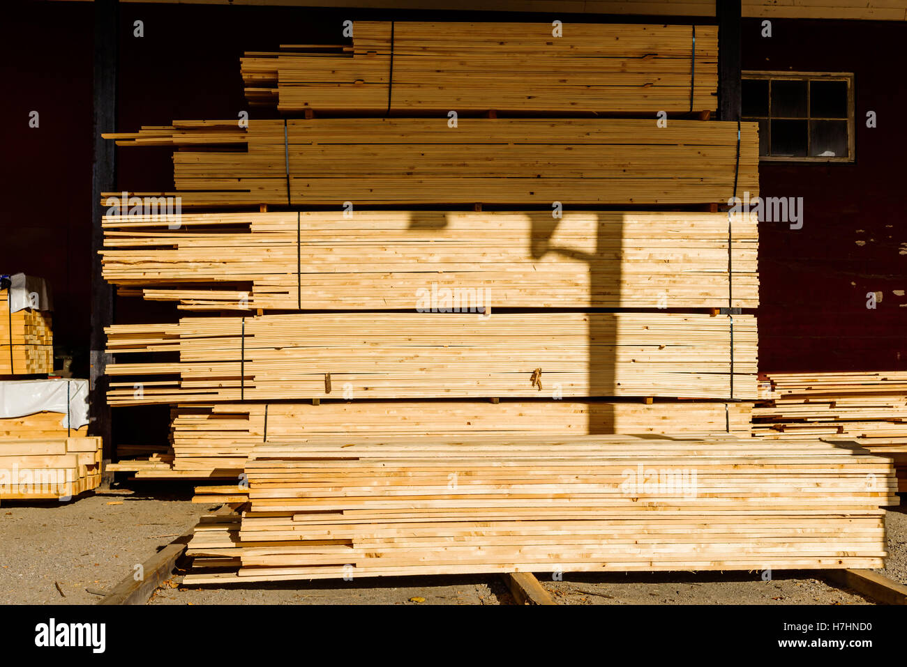 Stacks of thin planks stored outside a building partly shaded by the ...