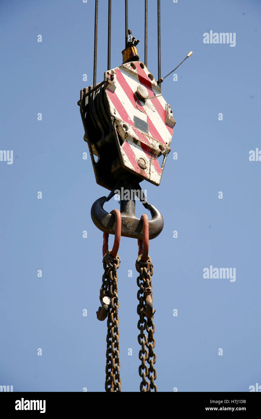 Long industrial crane chains with hooks hanging vertically against blue ...