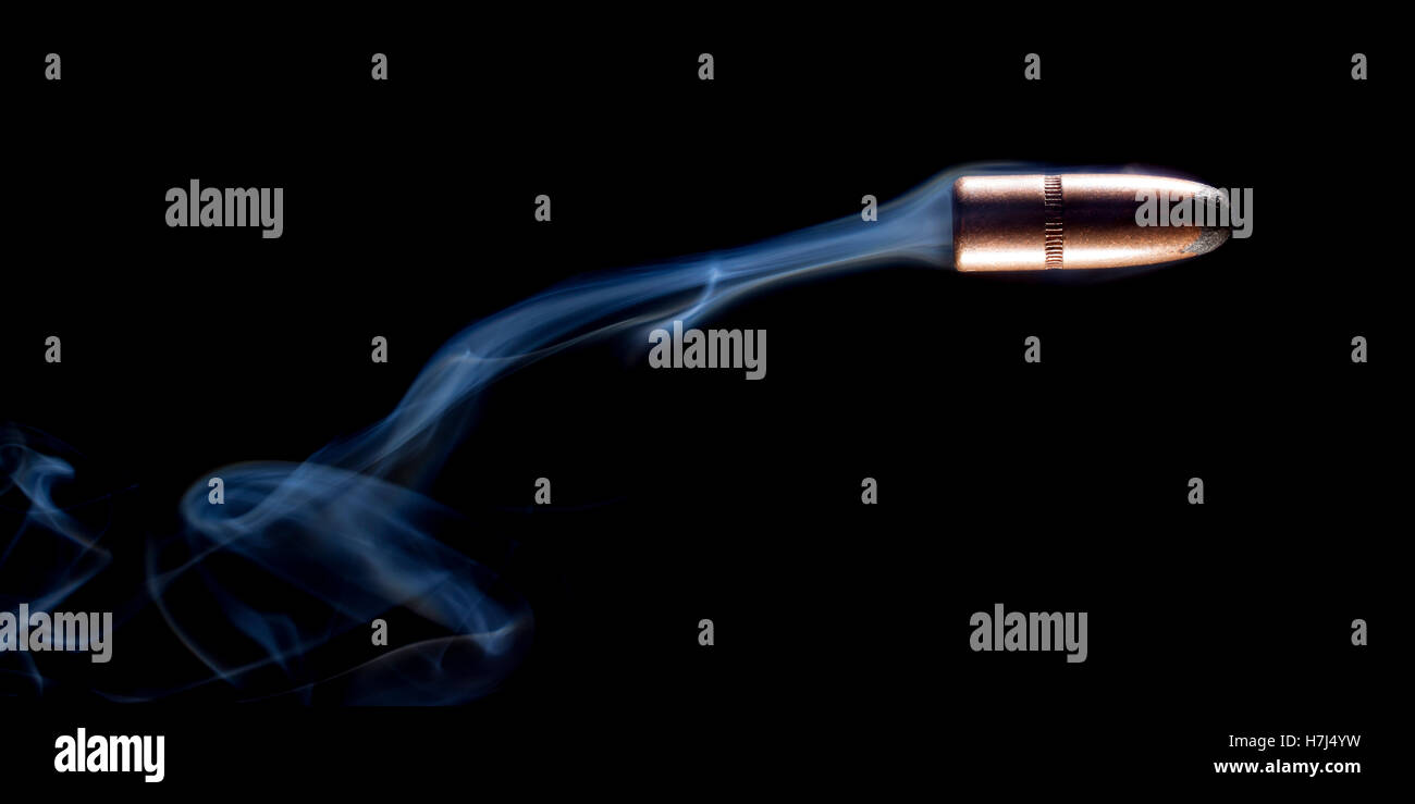 Copper colored bullet with a lead core on a black background with smoke ...