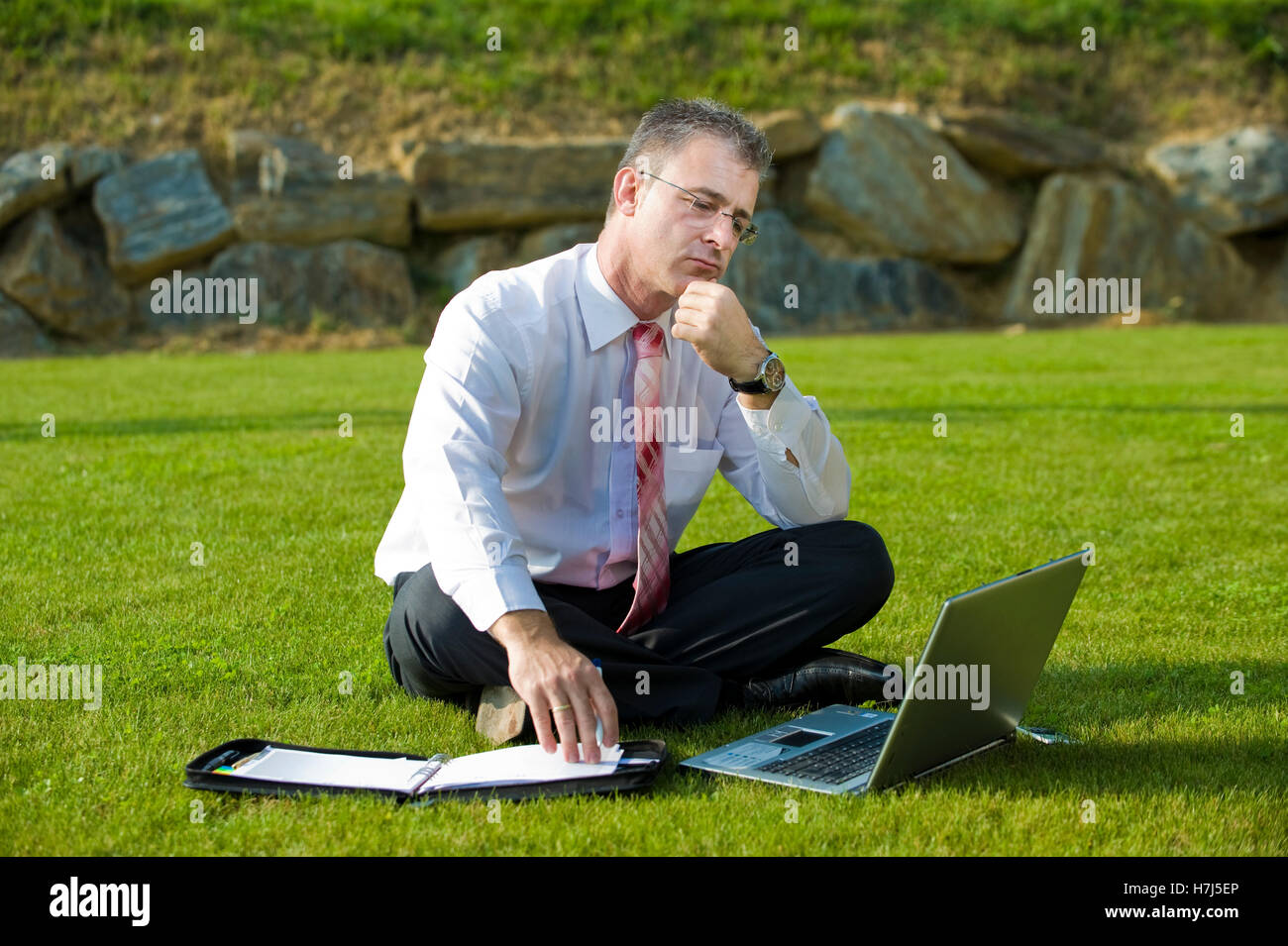 Businessman sitting in a park while using a laptop Stock Photo - Alamy