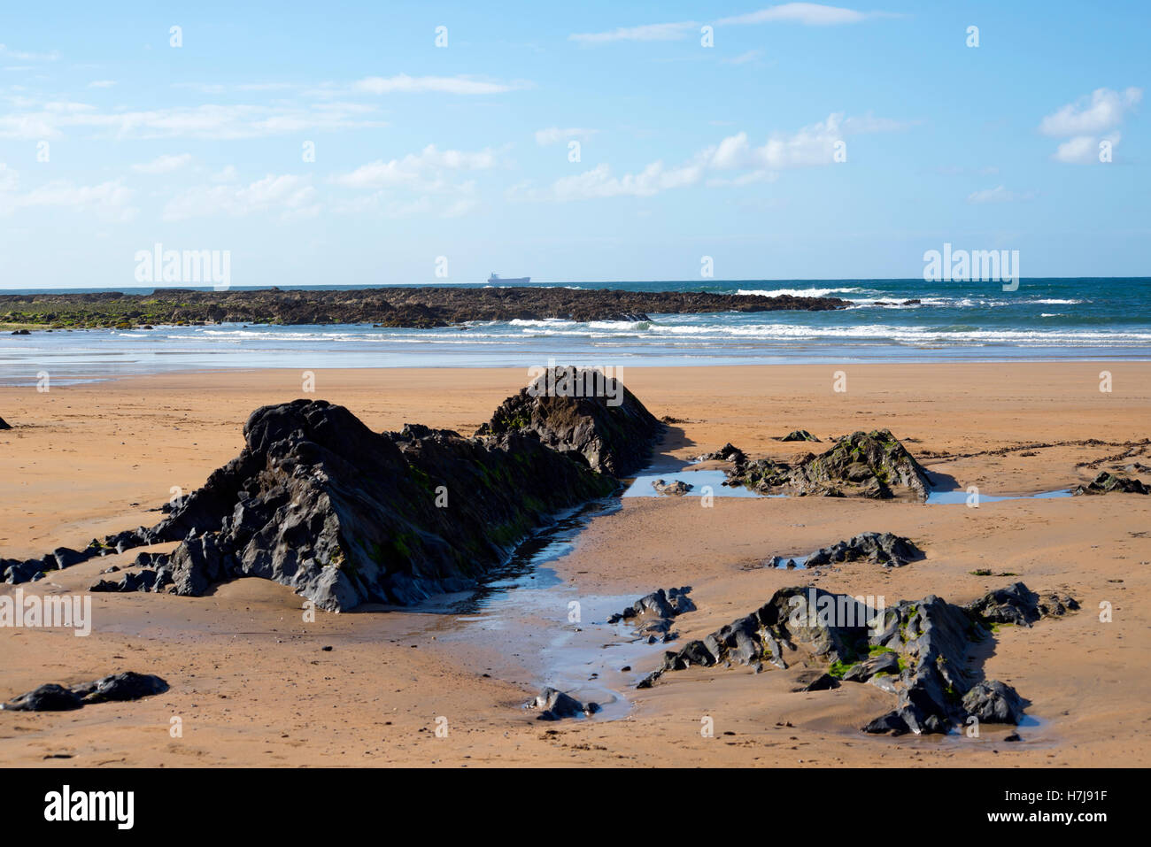 beautiful waves break on the black rocks at ballybunion with a tanker ...