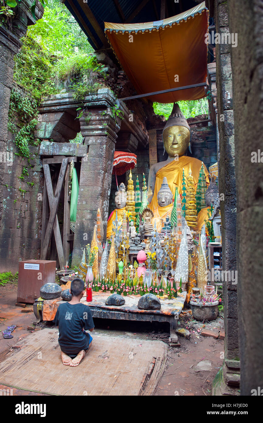 A young boy praying at a Buddhist shrine inside Wat Phu, a ruined Khmer ...