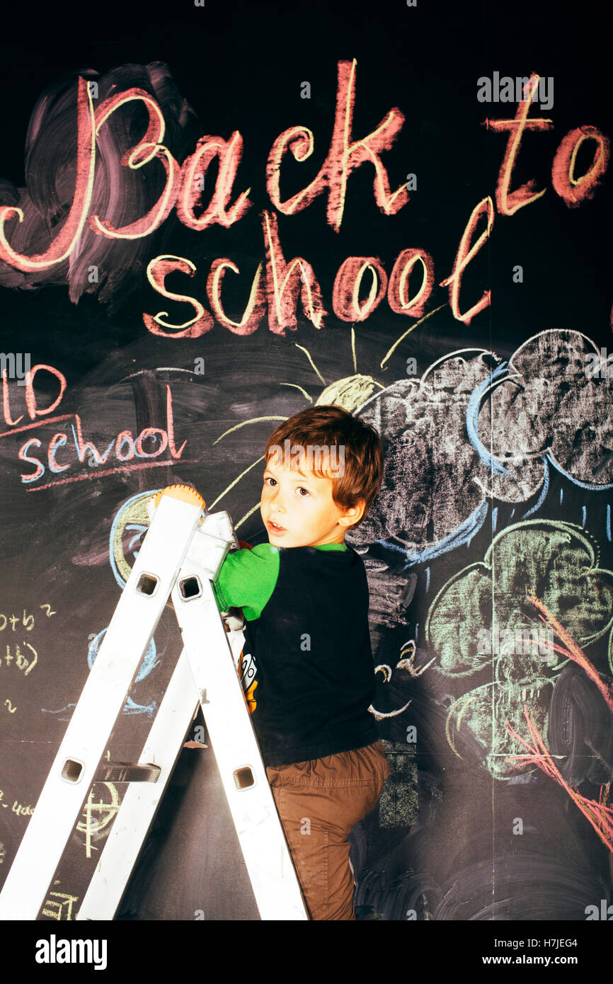 little cute real boy at blackboard in classroom, back to school concept ...