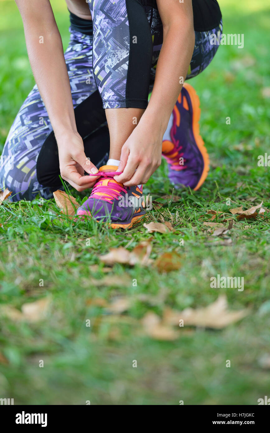 Female jogger tying laces on her shoes outside Stock Photo - Alamy