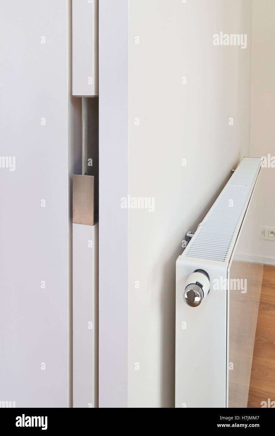 White radiator on wall with sliding door in an apartment with wooden ...