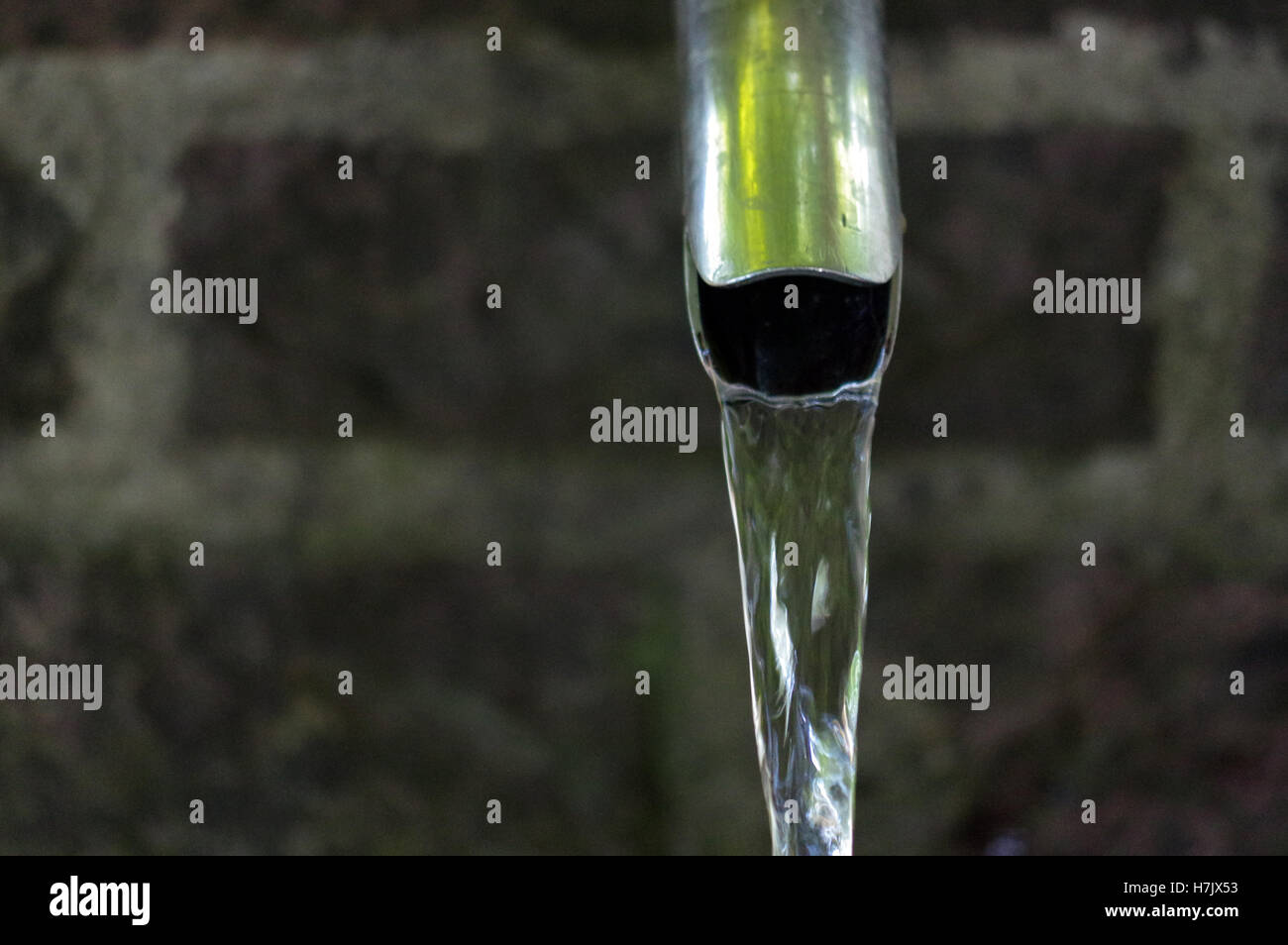 Close up of running water from a tap with brick wall on background ...