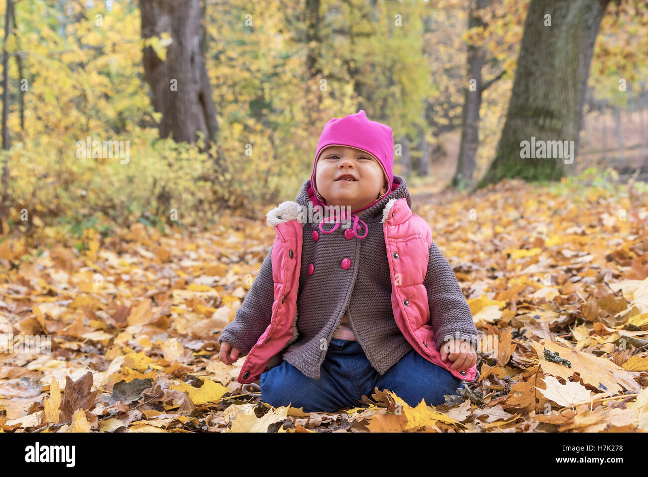 Happy baby girl in pink warm coat and pink hat makes grimace sitting on ...