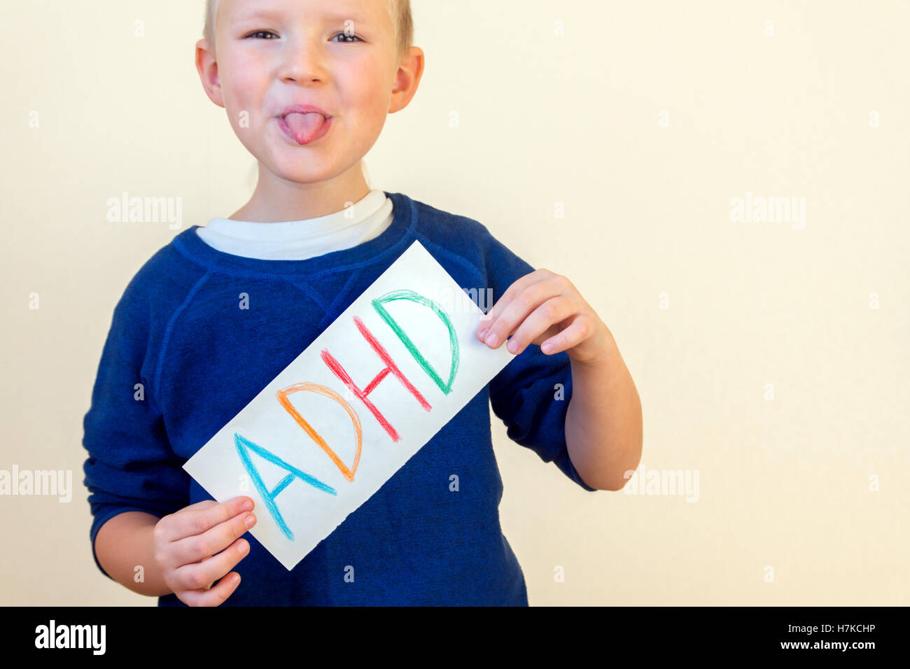 Young boy hold ADHD text written on sheet of paper and show his tongue ...