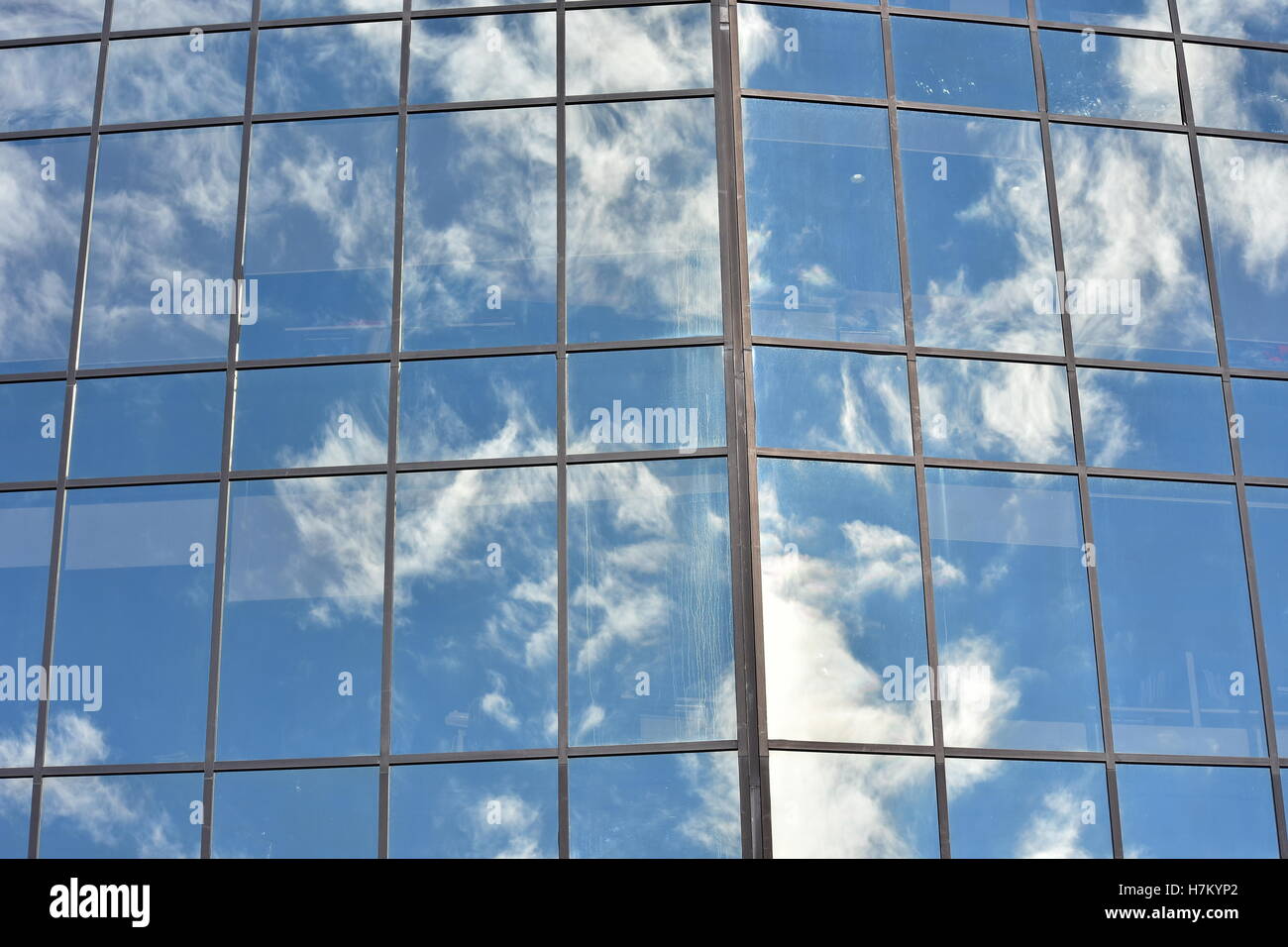 Glass facade of an office building reflecting the blue sky and clouds ...