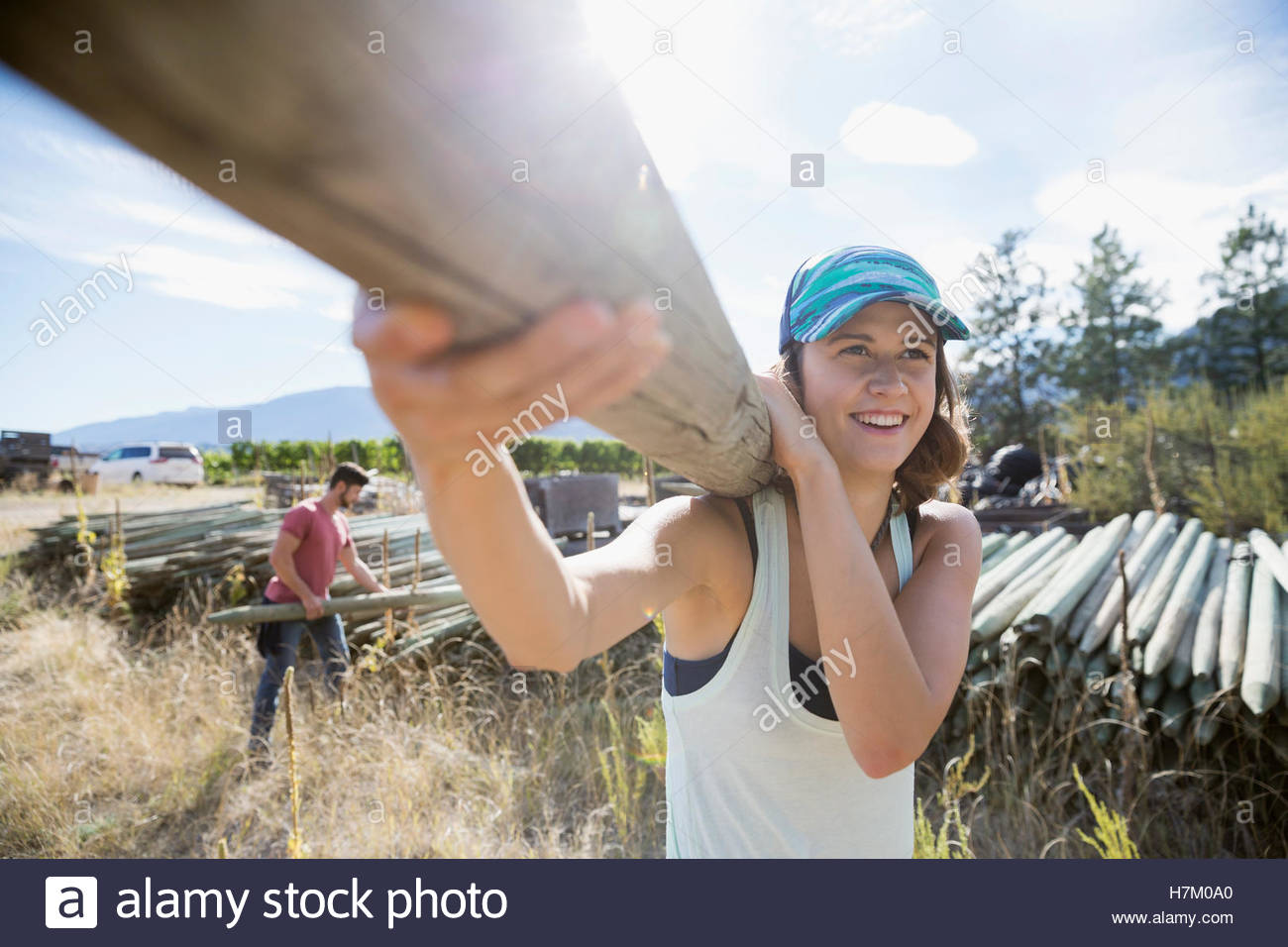Smiling female farmer carrying wood fence post on sunny farm Stock ...
