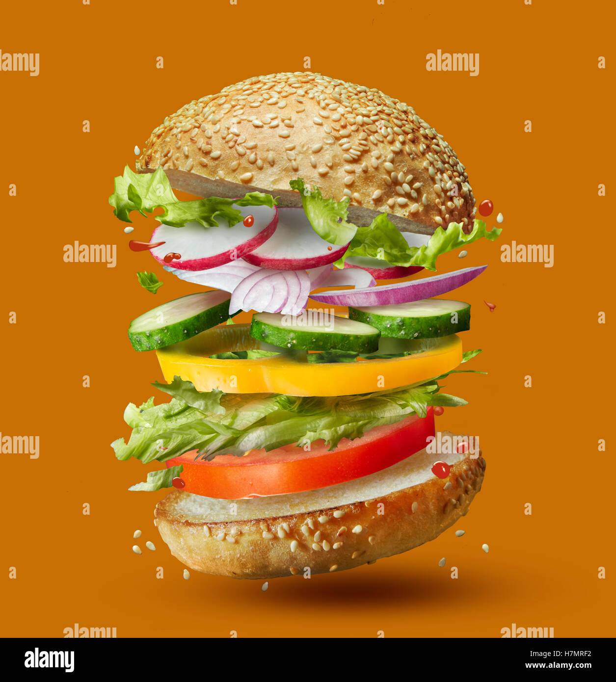 Burger preparation ingredients falling into place isolated on orange ...