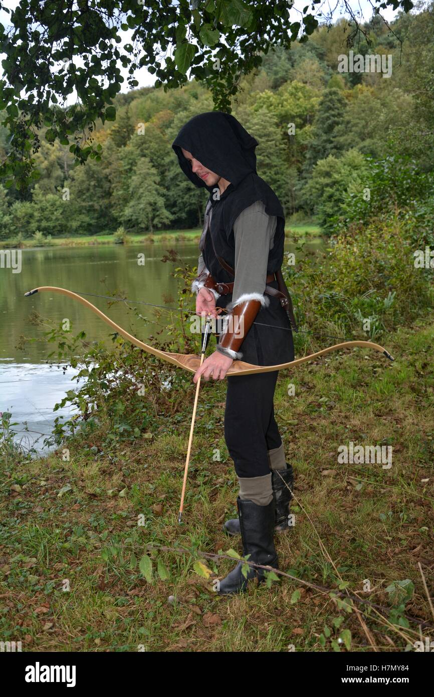 Medieval archer with black hood stands with tense curve and with arrows ...