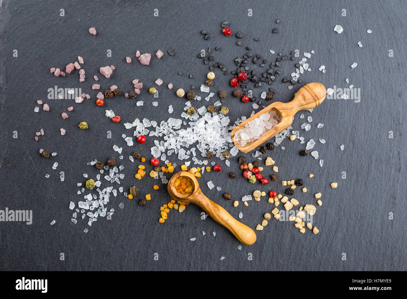 Different types of salt and pepper sprinkled on the stone background ...