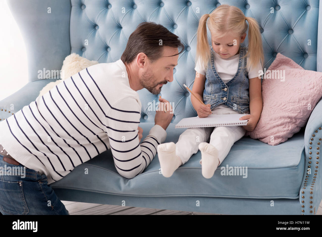 Handsome thoughtful father looking at the sketchbook of his daughter ...