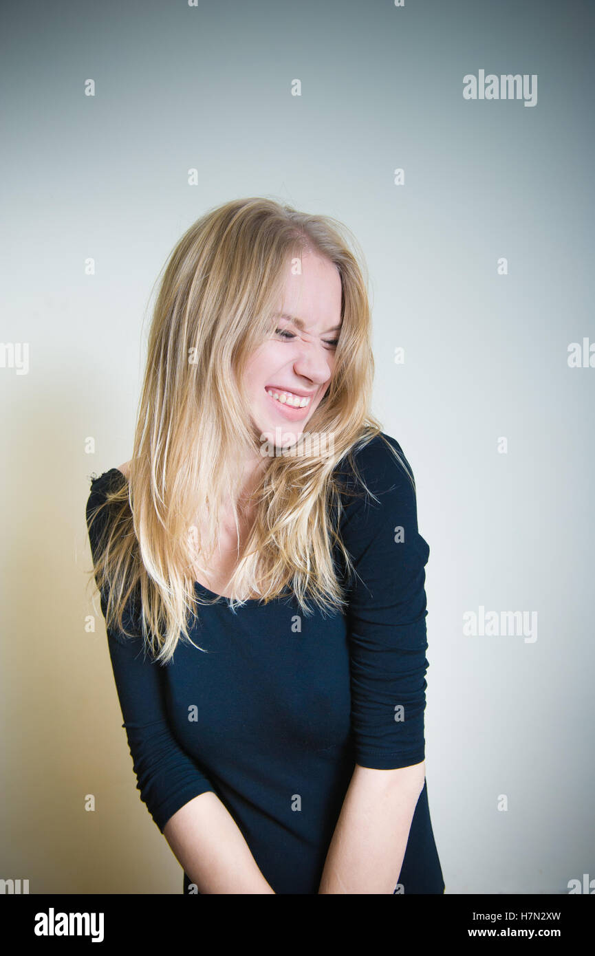 Young blonde woman, smirking with little grimace on white background ...