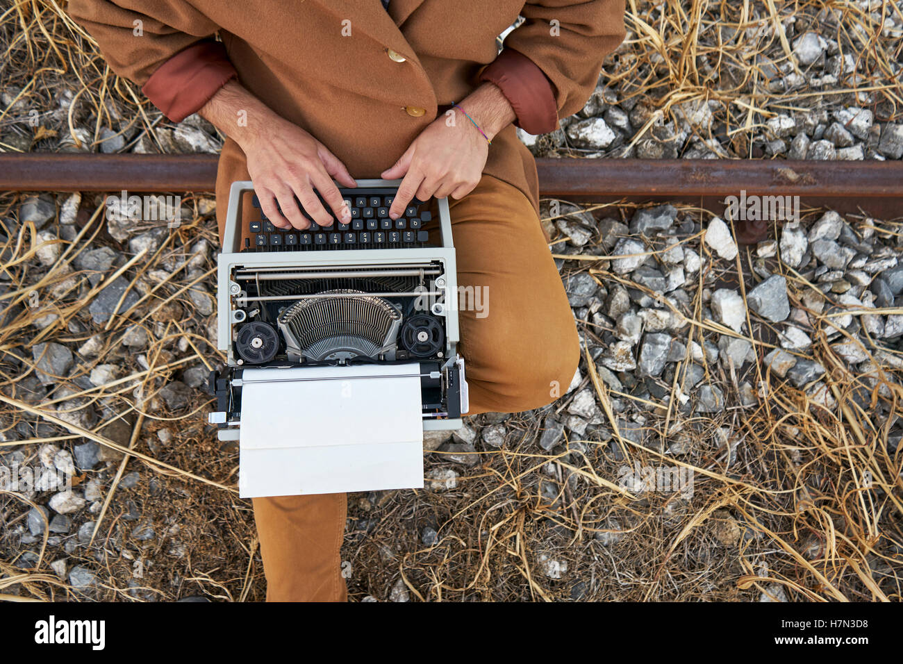 Concept with a man sitting in the train rail and typing on a typewriter ...