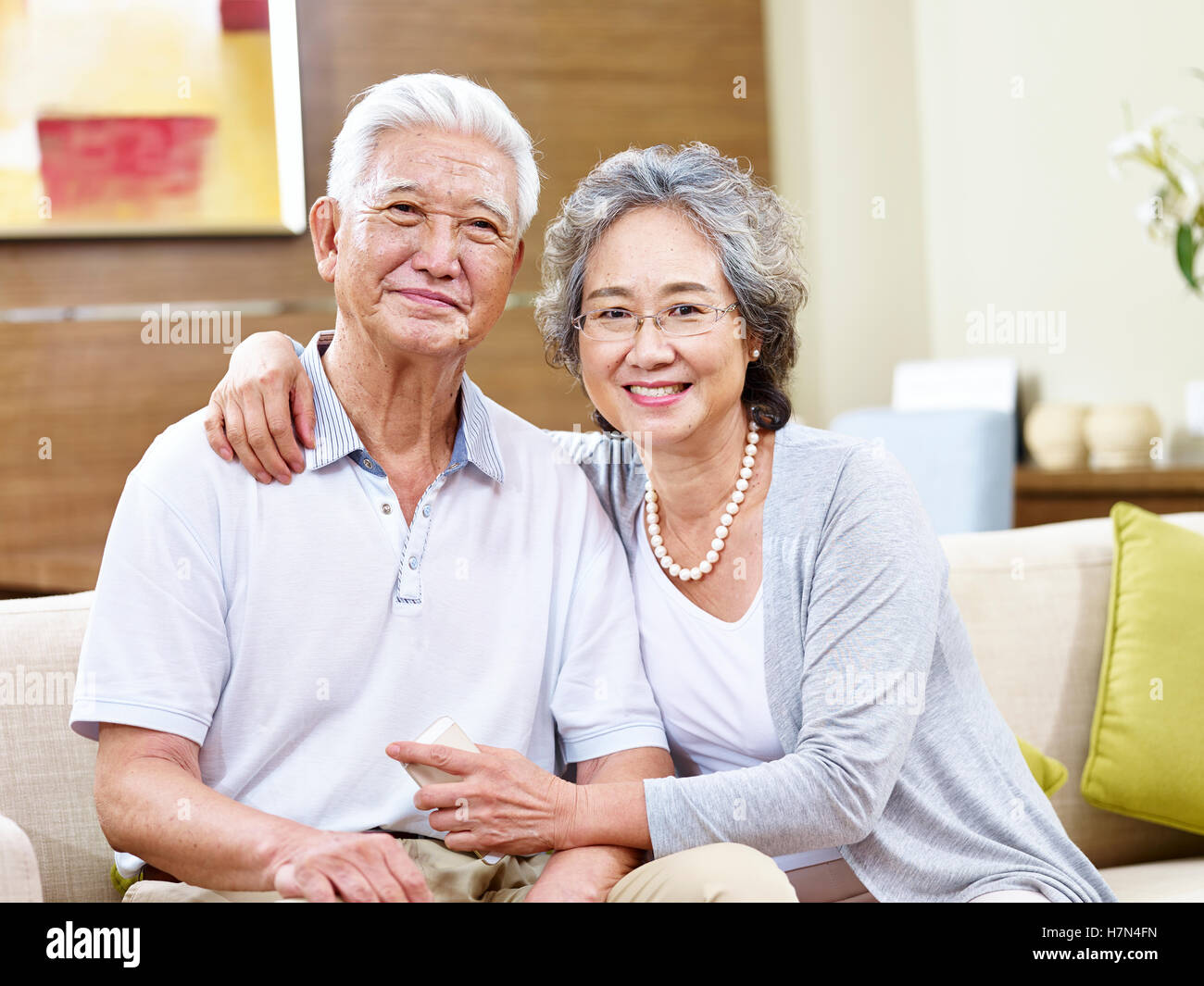 senior asian couple sitting on couch at home looking at camera smiling Stock Photo - Alamy