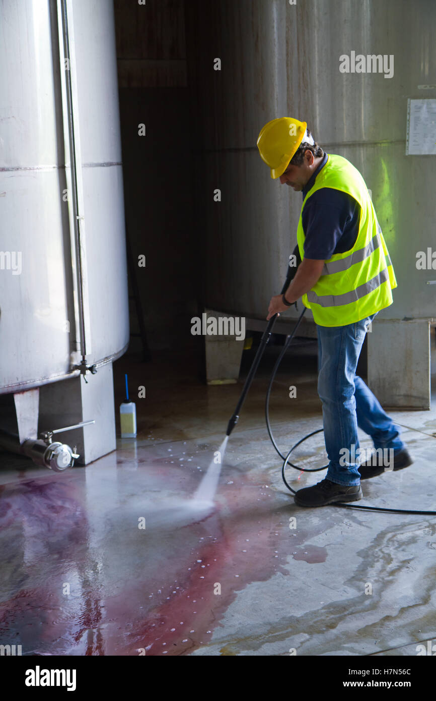 worker cleaning the floor with a pressure washer in a industrial site ...