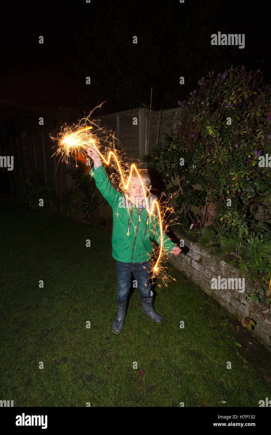 Boy (aged 5) in suburban backgarden with hand-held firework type ...