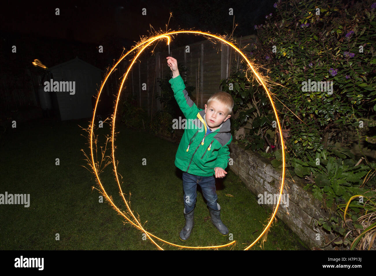 Boy (aged 5) in suburban backgarden with hand-held firework type ...