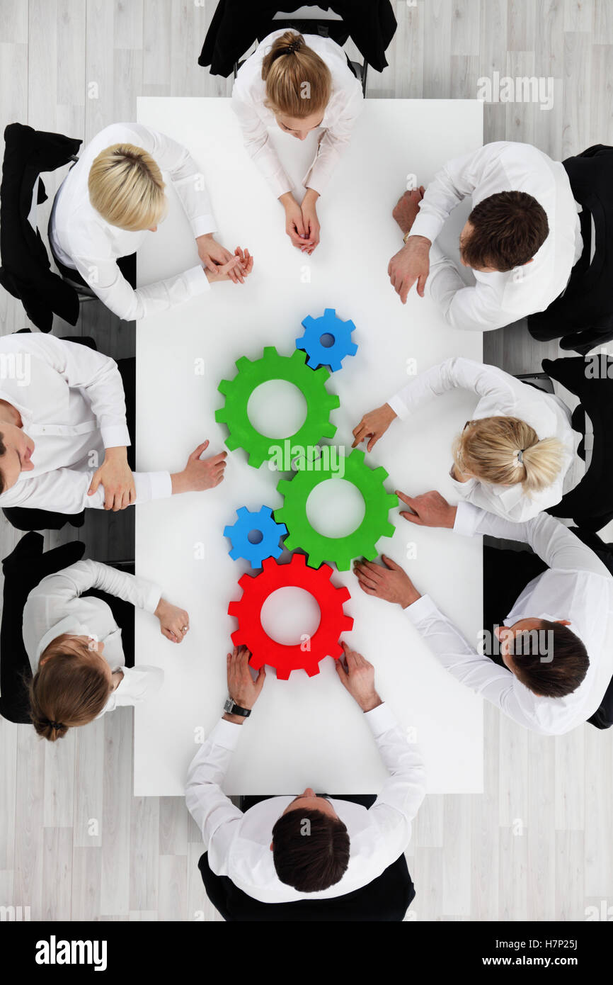 Business team sitting around the table with cogs, teamwork concept ...