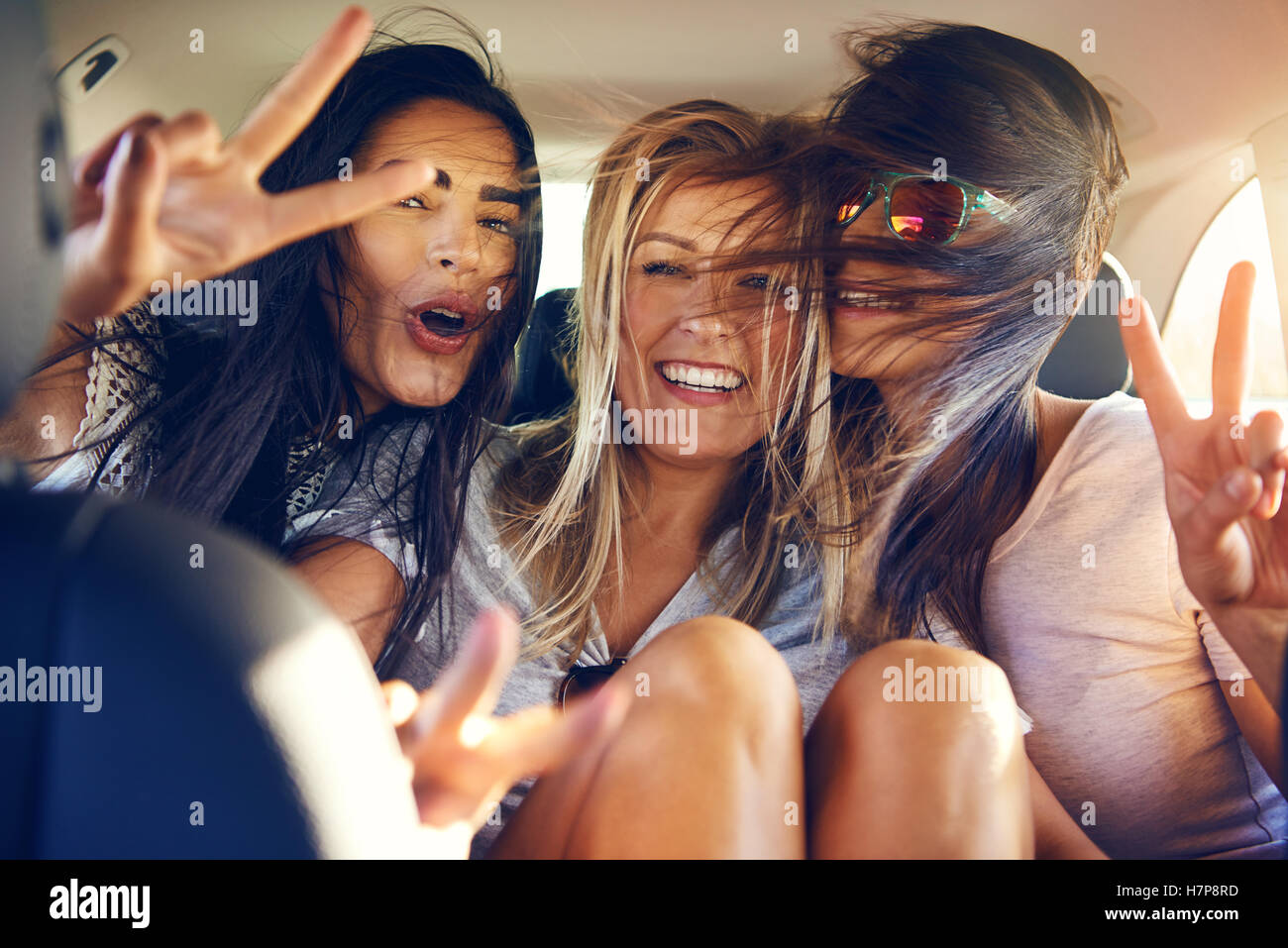 Three beautiful female friends make peace signs while seated in back ...