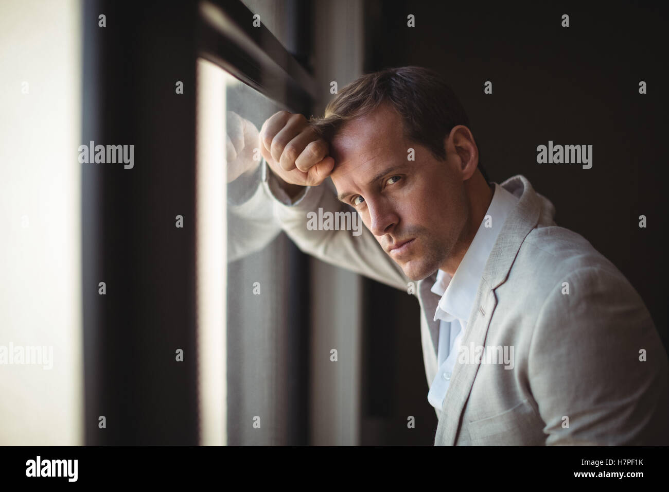 Thoughtful businessman leaning on window Stock Photo - Alamy