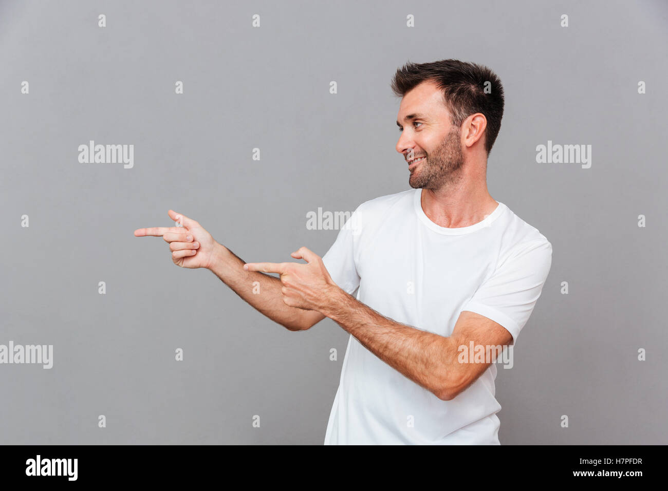 Portrait of a happy casual man pointing fingers away over grey ...