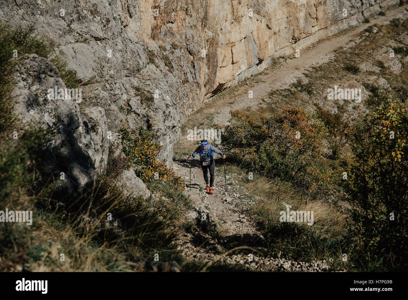 young male athlete with walking poles to walk uphill on background ...