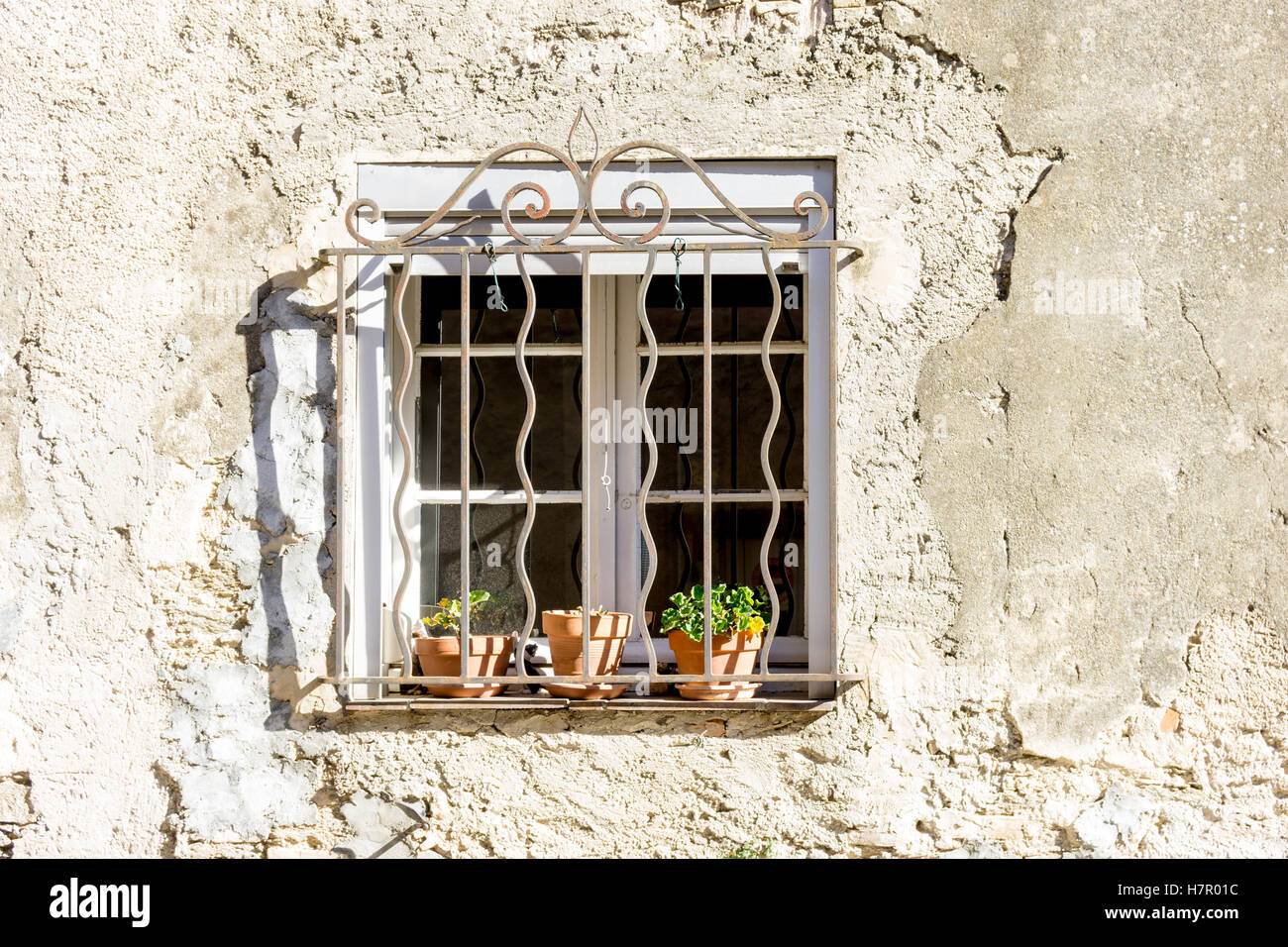A window with decorative bars and plants in pots set in an old ...