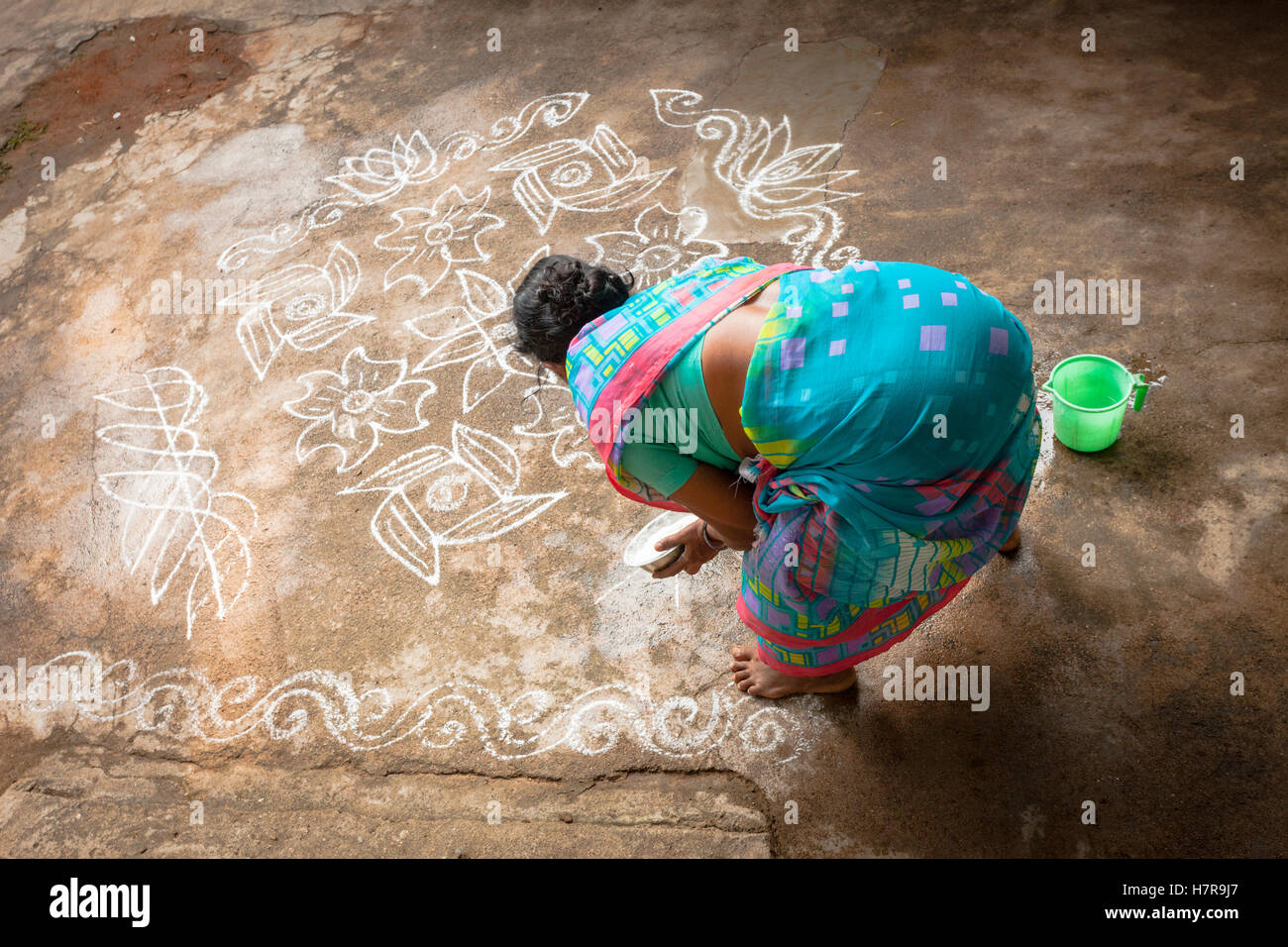 A woman makes a Rangoli drawing on the pavement outside her house ...