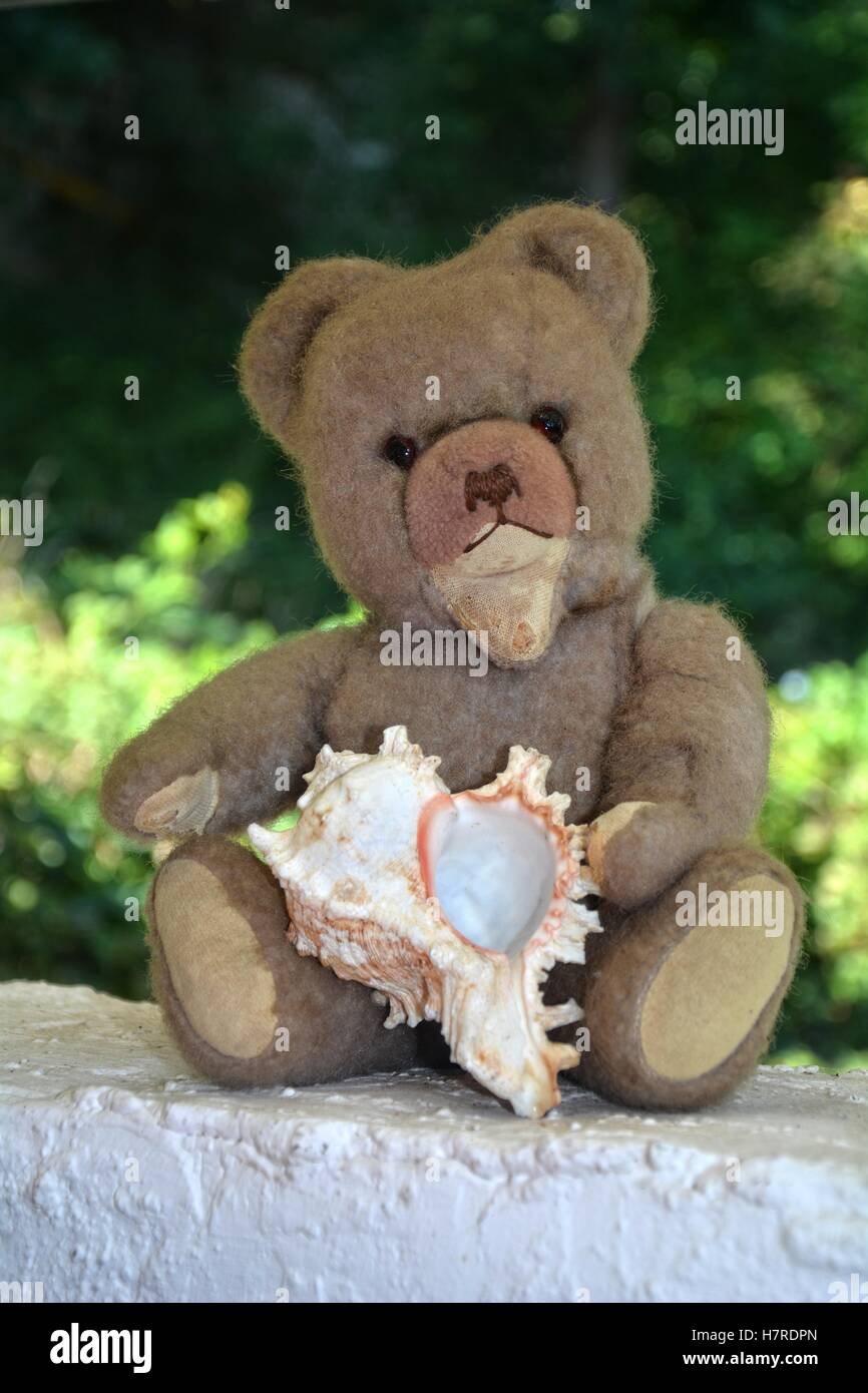 Teddy bear sits on a white wall against green nature background and ...