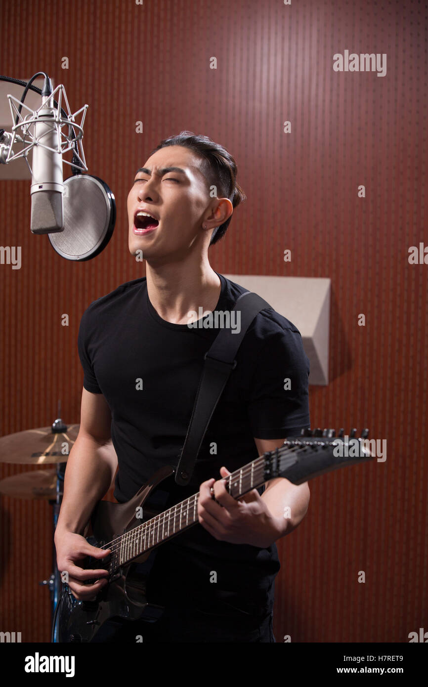 Young Chinese man singing with guitar in recording studio Stock Photo ...