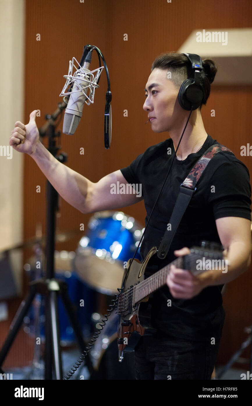Young Chinese man singing with guitar in recording studio Stock Photo ...