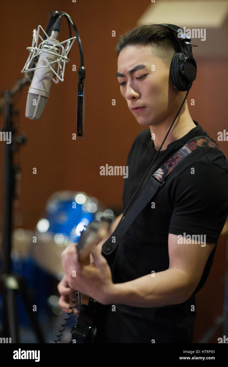 Young Chinese man singing with guitar in recording studio Stock Photo - Alamy