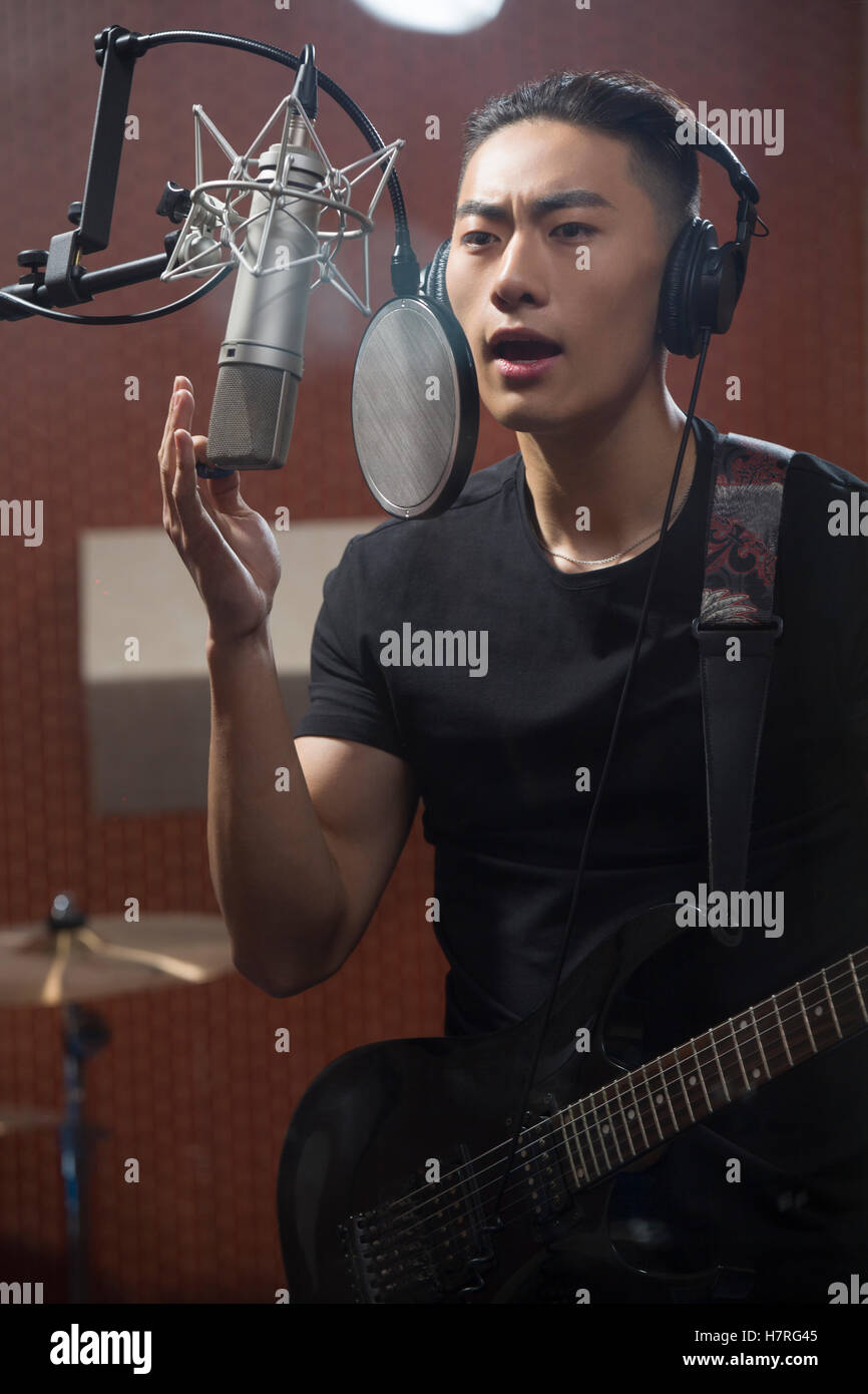 Young Chinese man singing with guitar in recording studio Stock Photo ...