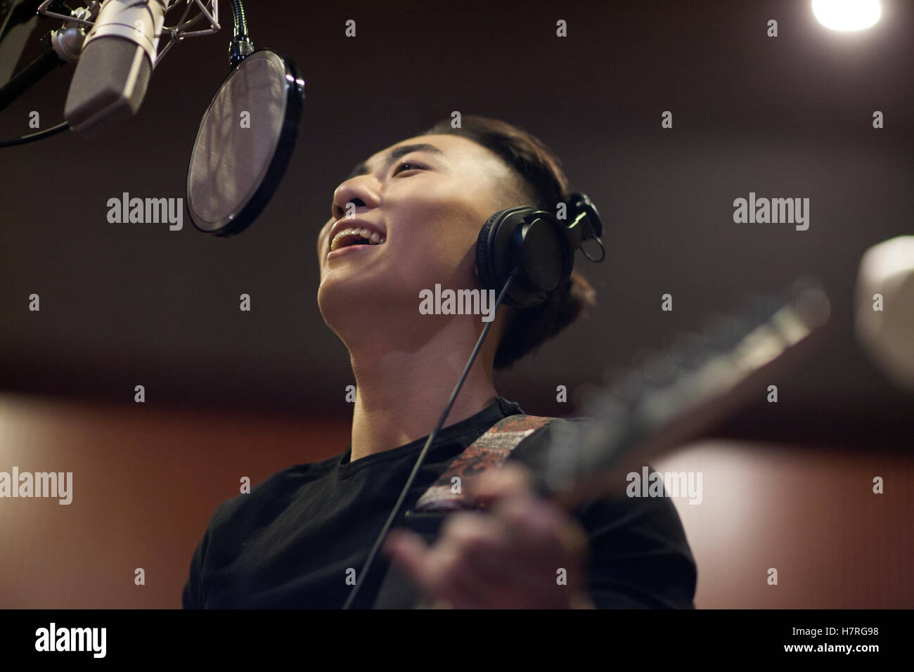 Young Chinese man singing with guitar in recording studio Stock Photo - Alamy