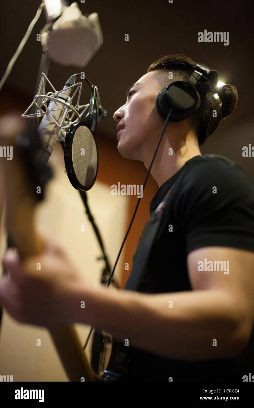 Young Chinese man singing with guitar in recording studio Stock Photo ...