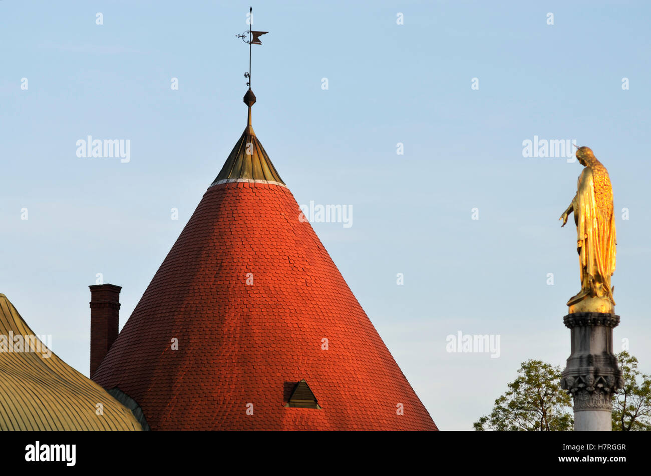 A peaked cone roof with weather vane and a gold statue against a blue ...